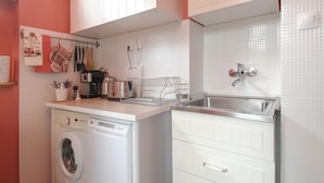 Cozinha compacta com máquina de lavar, cafeteira e pia.