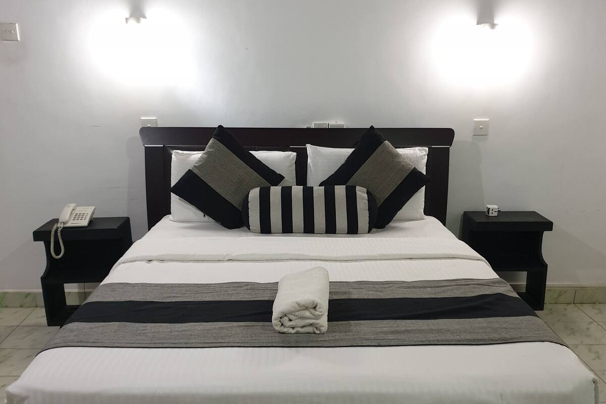 Cama bem arrumada com travesseiro listrado, toalha dobrada e telefone de mesa.