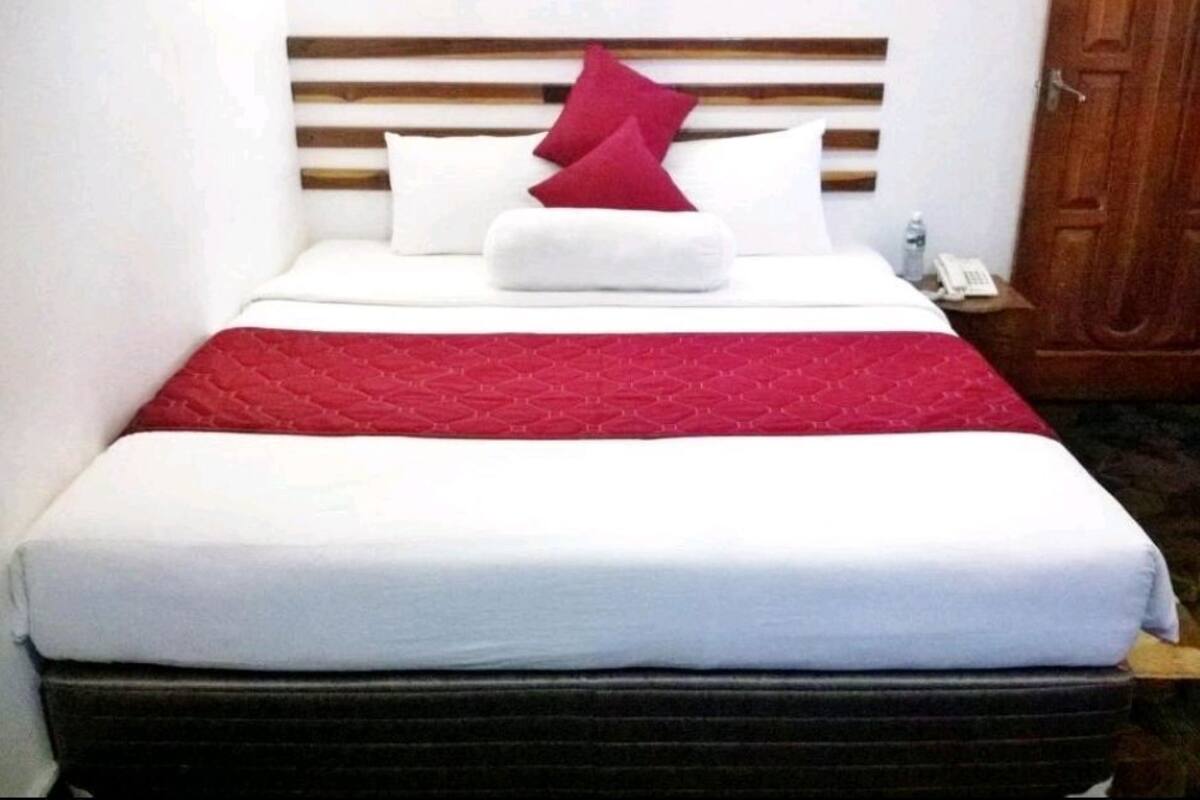 Uma cama com colchão branco, manta vermelha e dois travesseiros.
