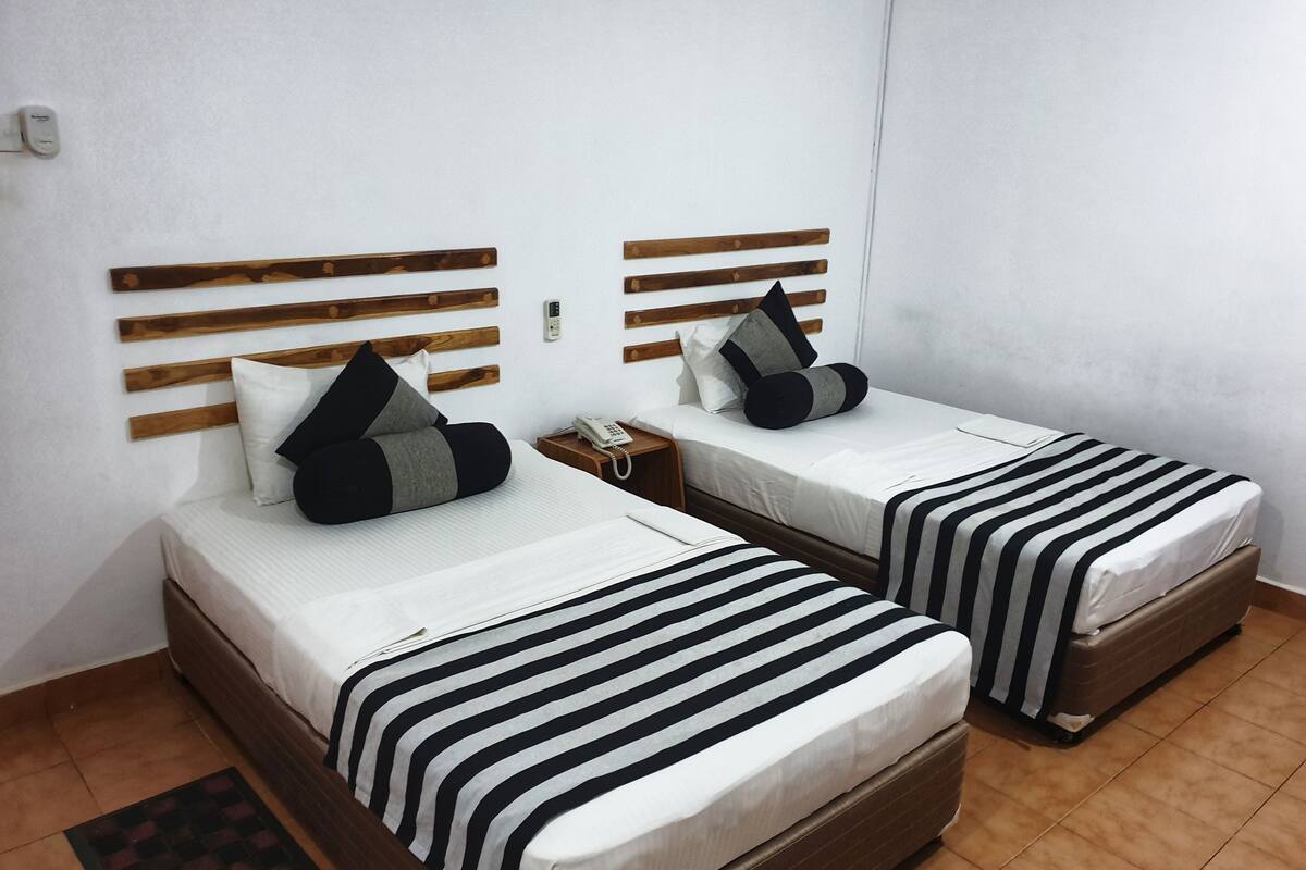 Duas camas de solteiro com roupa de cama listrada, cabeceiras de madeira e telefone ao lado da cama.