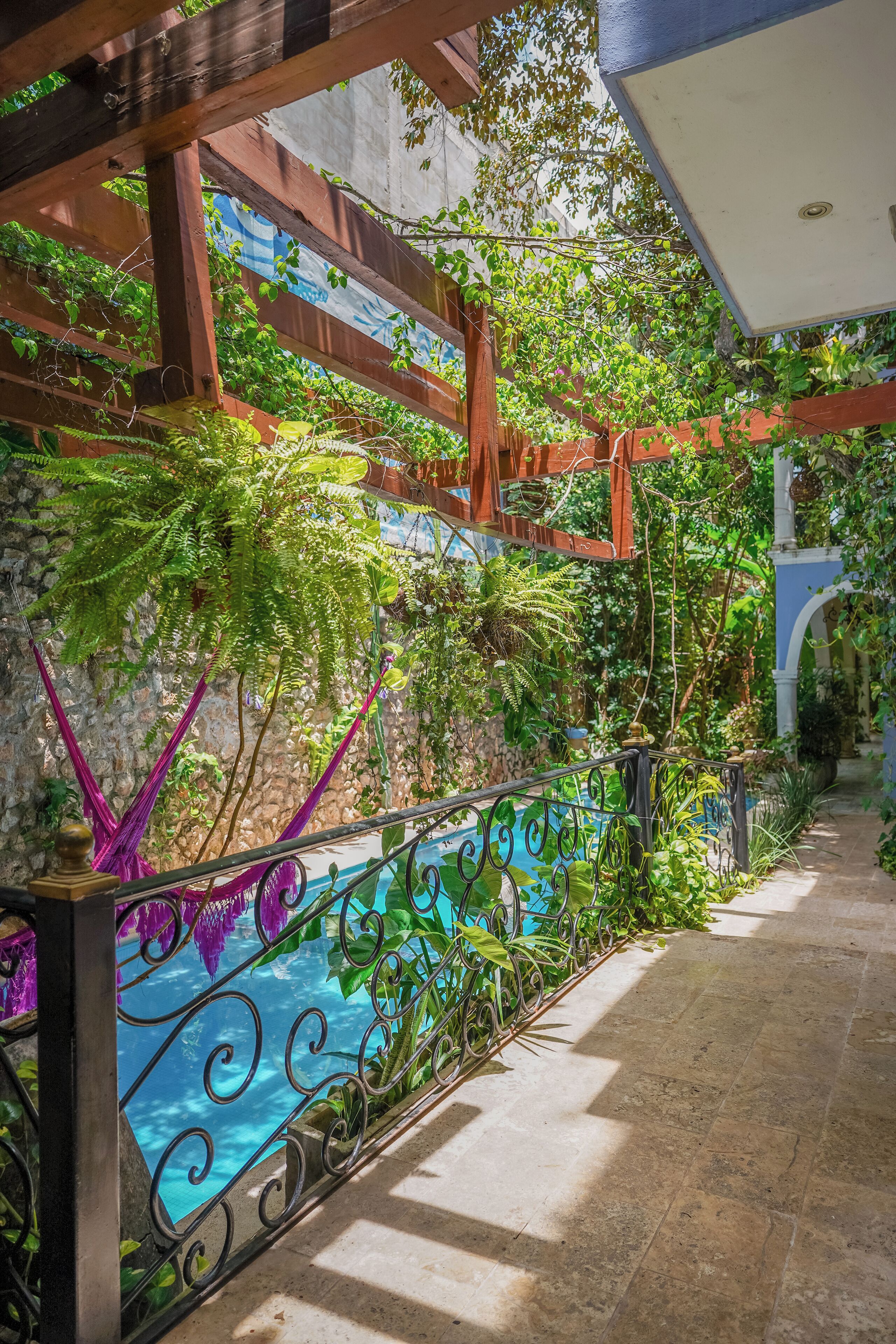 Uma área externa coberta com piso de azulejos, guarda-corpo de metal e vegetação exuberante.