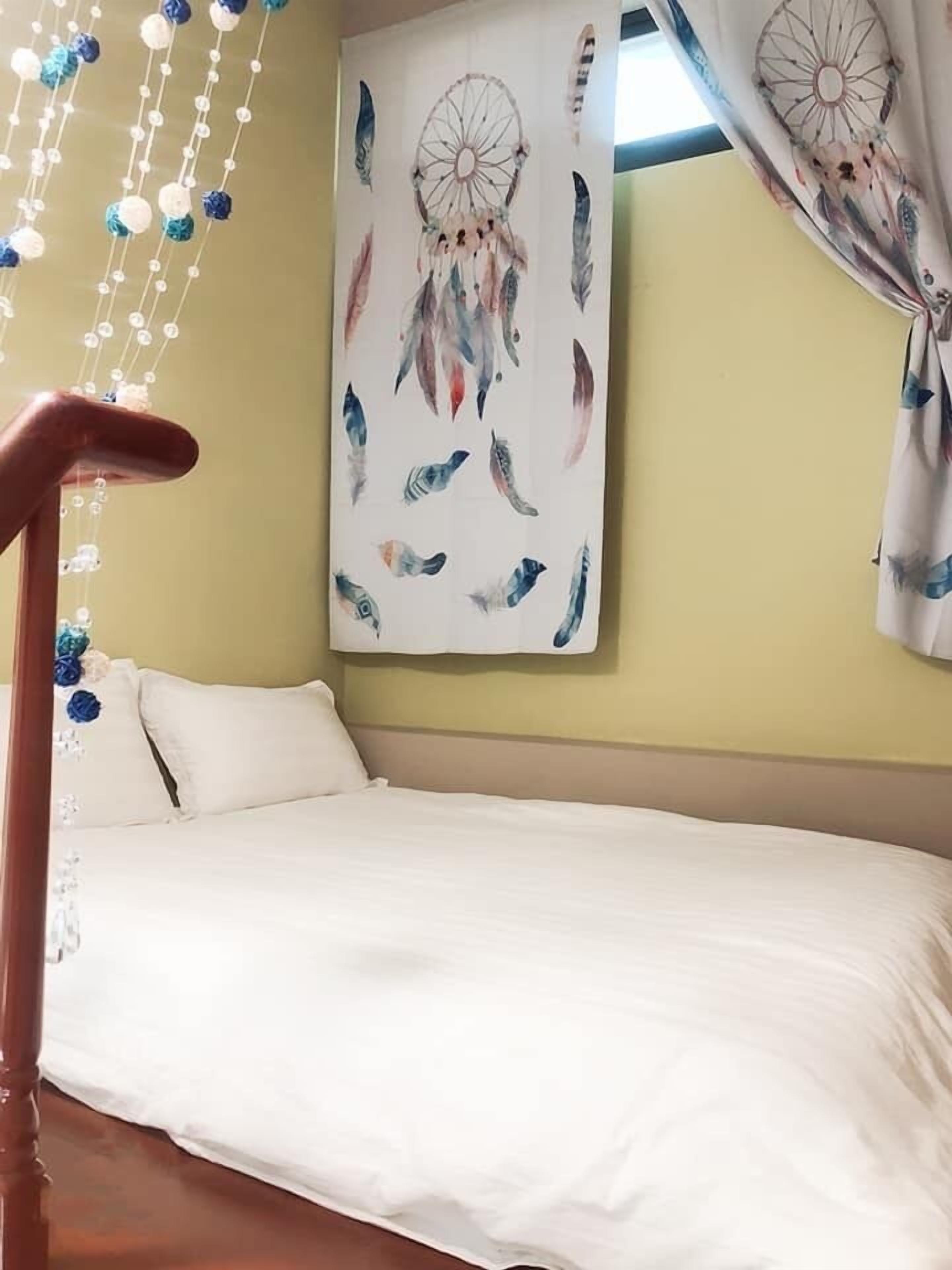 Uma cama com roupa de cama branca, uma parede com pintura de sonho e uma cortina com padrão floral.