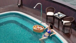 Piscina com borda azulejada, uma espreguiçadeira, uma mesinha com um vaso e uma cesta de objetos.