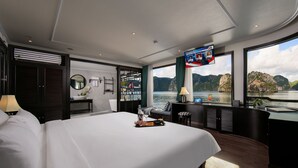 Quarto de hotel moderno com uma cama grande, uma mesa de trabalho, televisão e vista para um lago e montanhas.