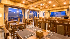 Um restaurante com interiores em madeira, mesas preparadas com talheres e grandes janelas com vista.