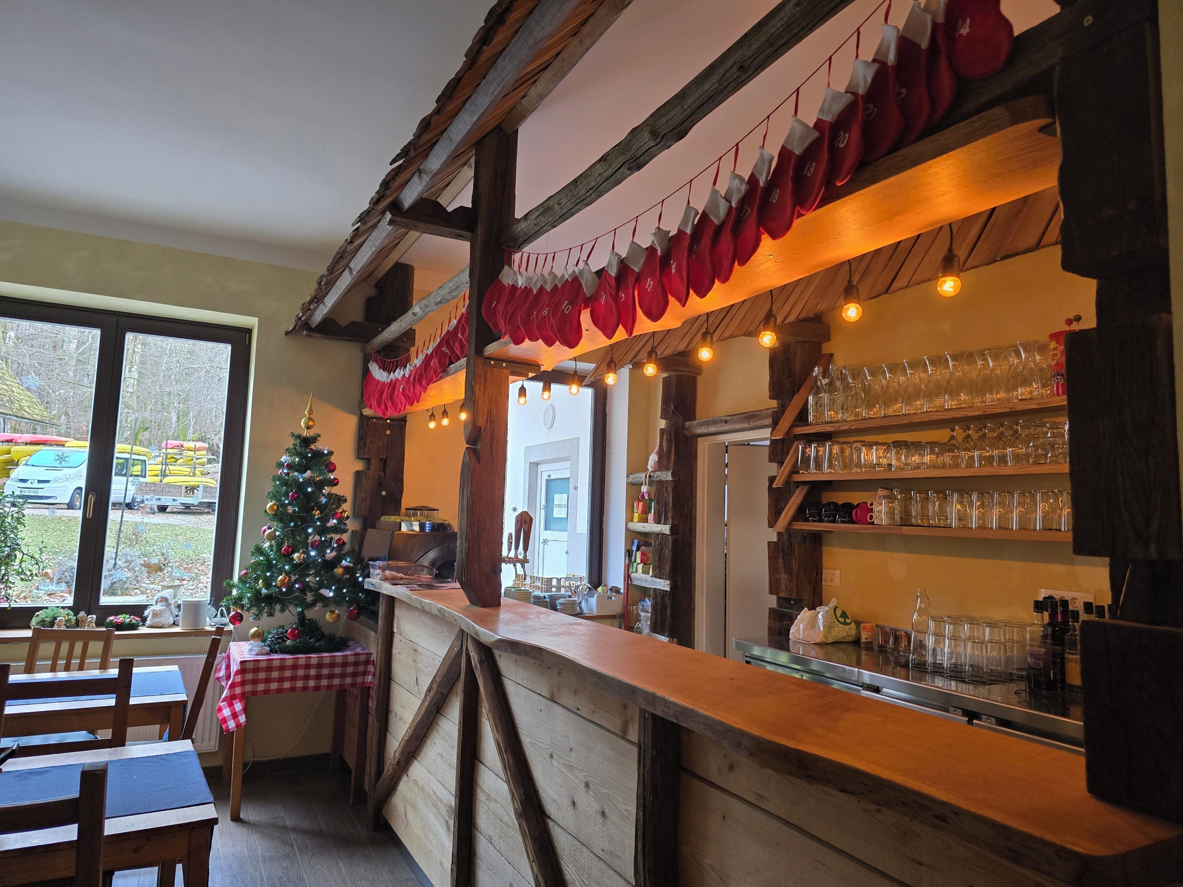 Um interior rústico com vigas de madeira, um pinheiro de Natal e um espaço de bar com copos e garrafas.