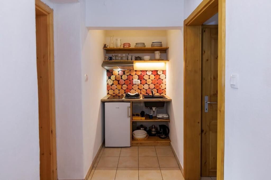 Cozinha compacta com geladeira, prateleiras de madeira e um painel de objetos circulares.