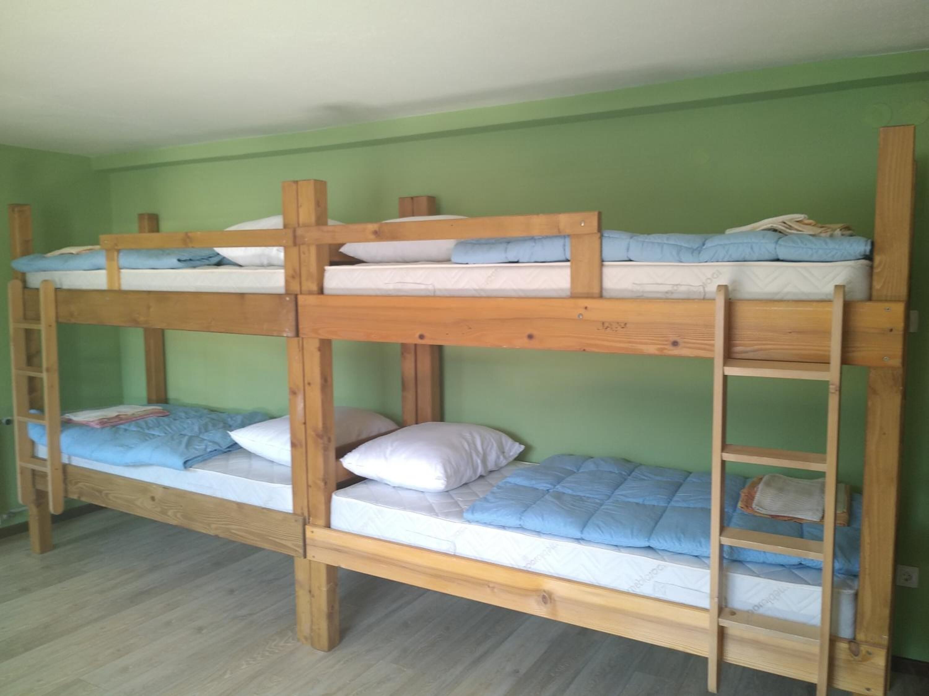 Uma cama de beliche com três andares, estrutura de madeira e uma escada do lado direito.