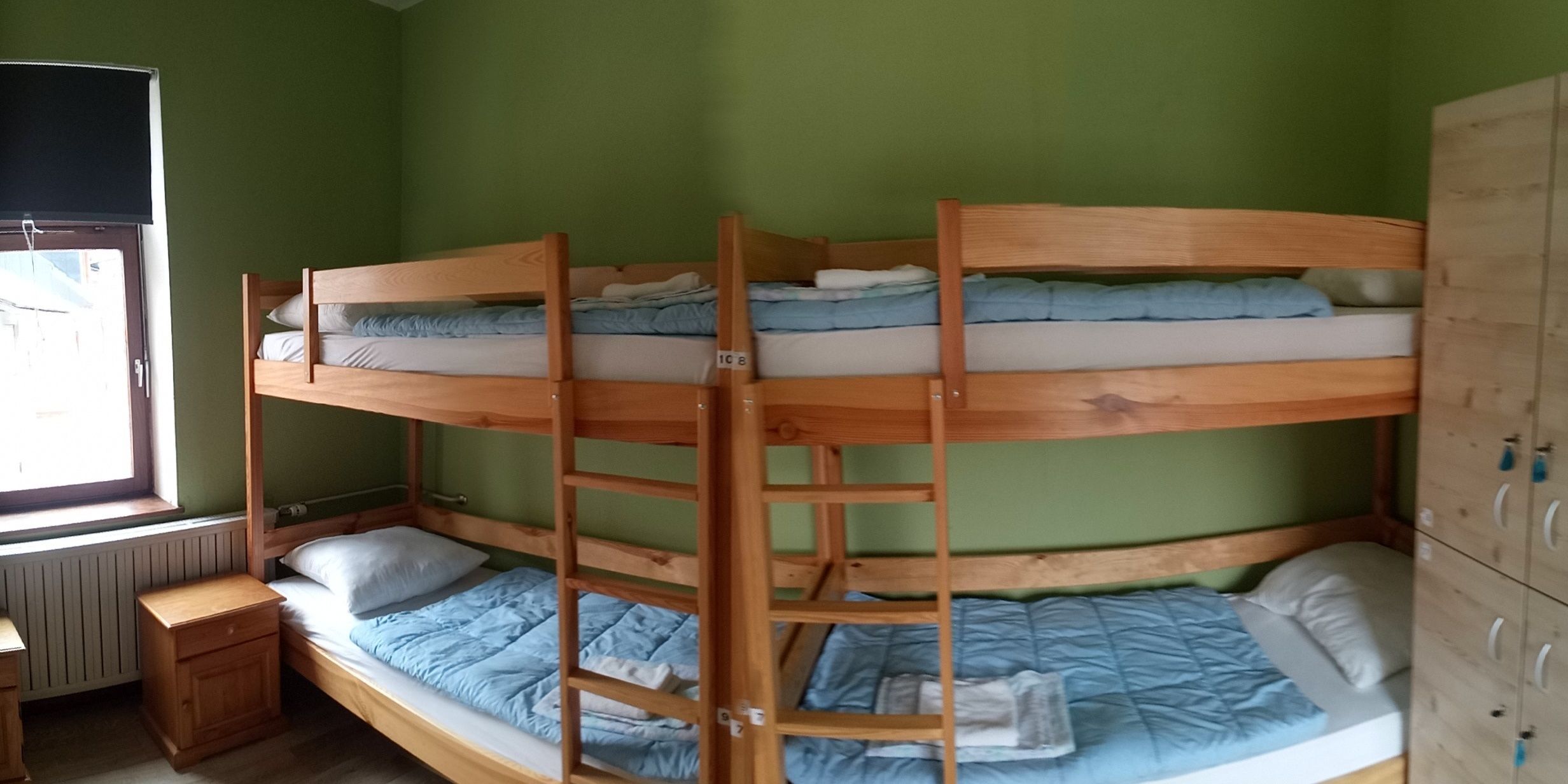 Quarto com beliche, janela, pequeno armário de madeira e radiador.