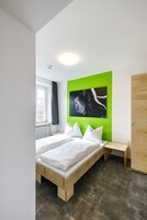 Quarto moderno com uma cama grande, mesa de cabeceira, um banco, parede verde e uma obra de arte em preto e branco.
