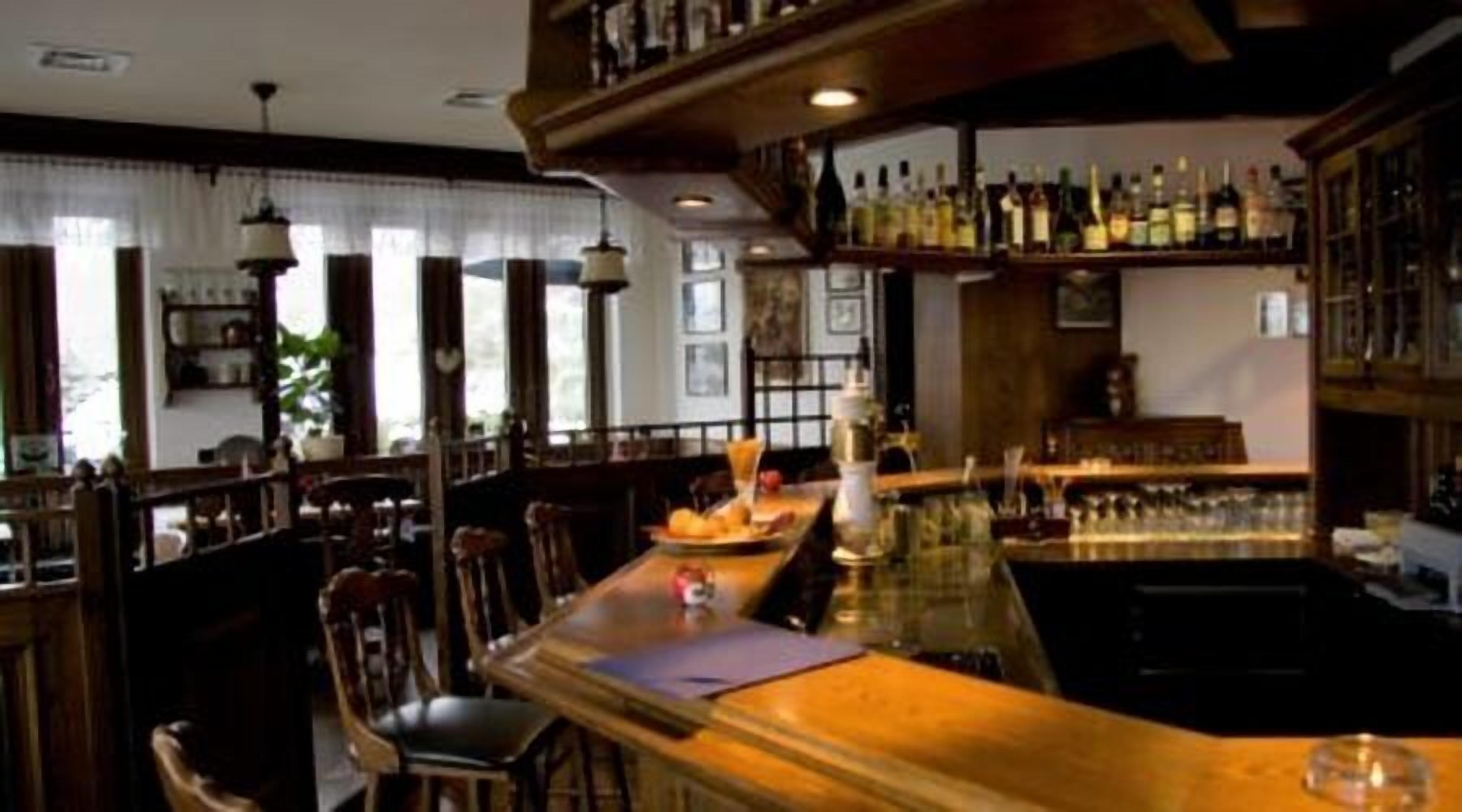 Uma área de bar com móveis de madeira, balcão alto e diversos frascos em prateleiras.
