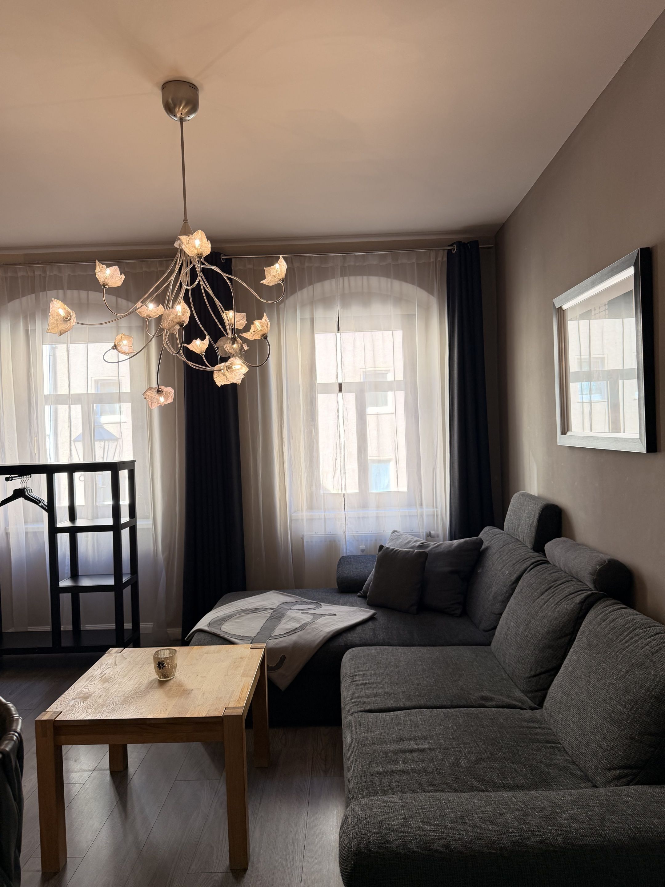 Uma sala de estar moderna com um sofá cinza, uma mesa de centro de madeira e um candelabro exclusivo.