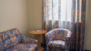 Um quarto com um sofá azul estampado, uma poltrona combinando, uma mesa redonda pequena e uma janela com cortinas estampadas.