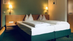 Quarto de hotel com cama de casal, duas luminárias de cabeceira, mesa de cabeceira e uma porta.