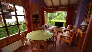 Um quarto aconchegante com uma mesa redonda de vidro cercada por cadeiras de madeira, um sofá e uma televisão.