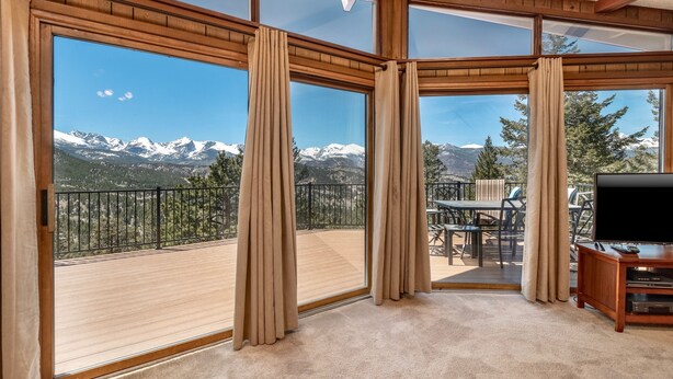 Quarto com grandes janelas com vista para as montanhas, varanda com deck de madeira e um rack para TV.