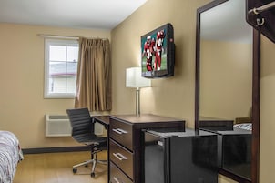 Quarto de hotel com cama, escrivaninha, cadeira, televisão fixada na parede e janela com cortinas.
