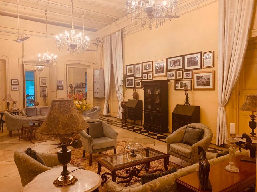 Uma sala de estar ampla, com lustre, poltronas, mesa de centro e lareira.