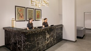 Balcão de recepção com tampo de mármore, duas obras de arte emolduradas acima e uma luminária moderna.