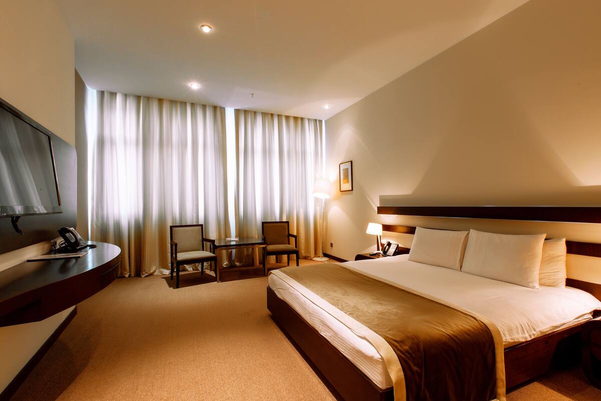 Quarto de hotel com uma cama grande, uma escrivaninha, uma cadeira e uma televisão.