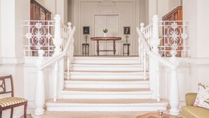 Uma escadaria imponente com balaústres brancos que leva a um patamar com mesa e cadeiras.