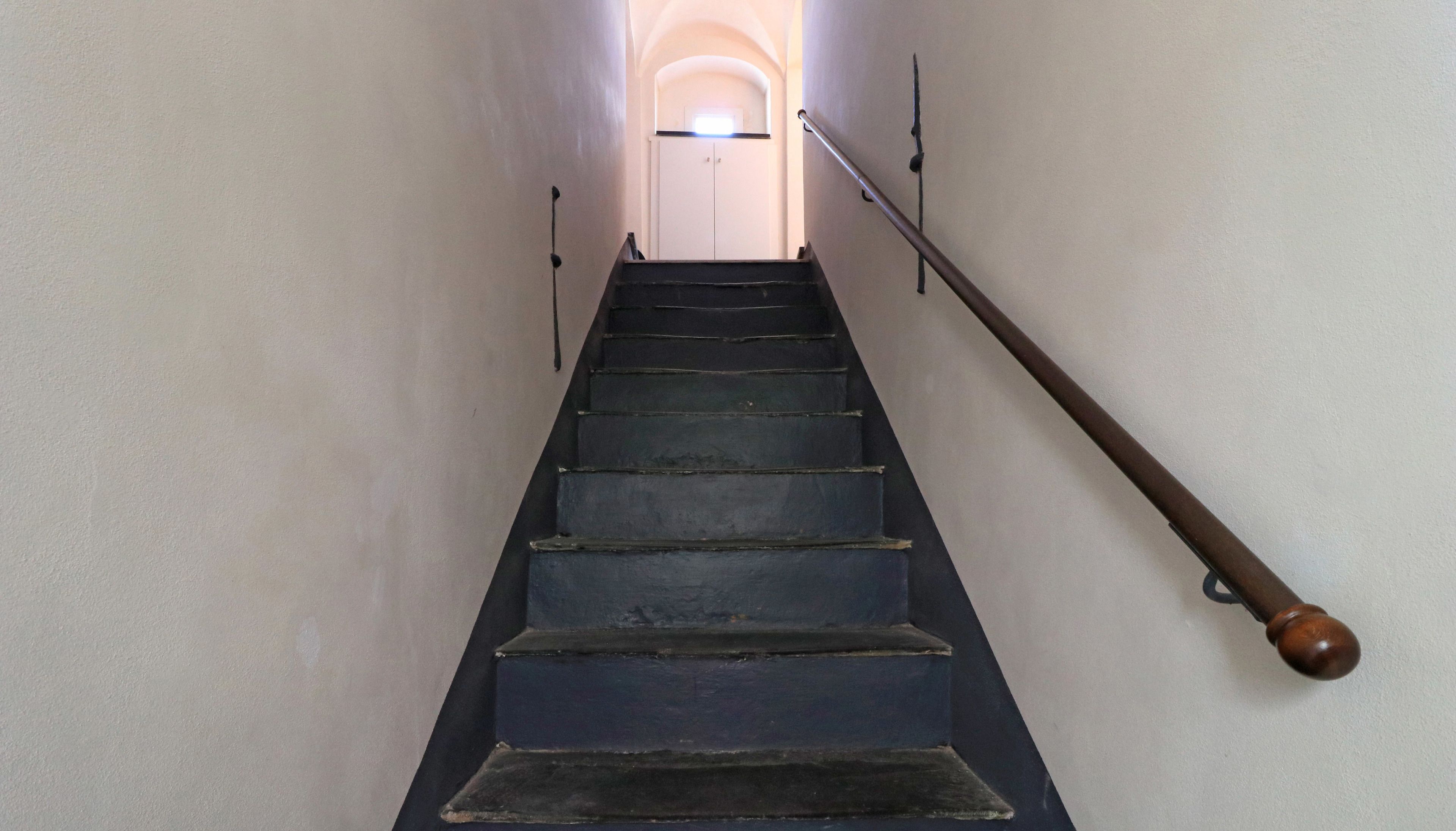 Uma escadaria com corrimão de madeira que leva a uma porta no topo.