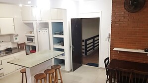 Uma cozinha moderna com armários brancos, uma ilha central com banquetas, micro-ondas e frigorífico.