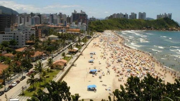 Uma praia com uma fileira de edifícios ao longo da costa, areia dourada e o oceano.