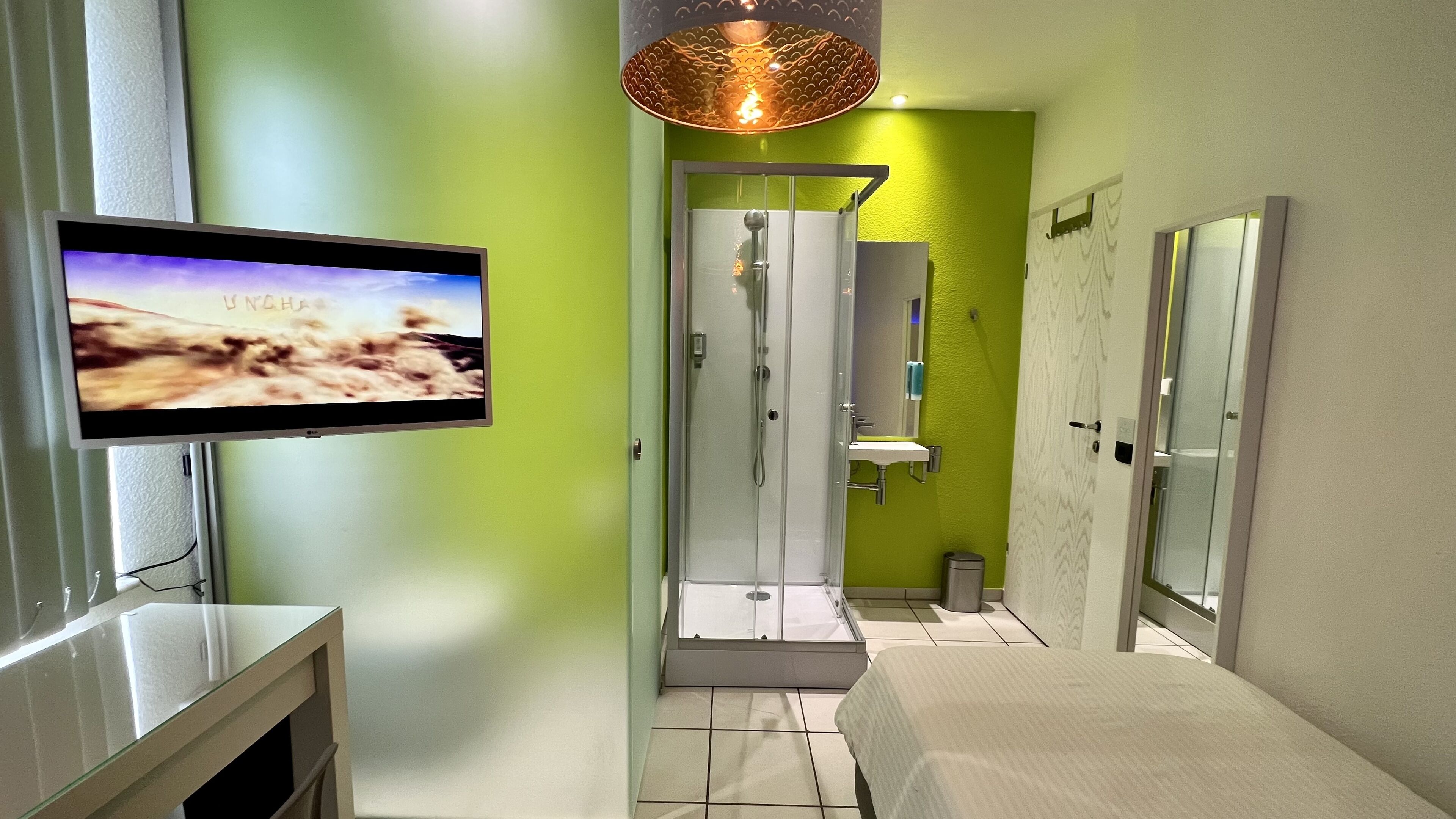 Quarto de hotel moderno com televisão, chuveiro, pia e cama.