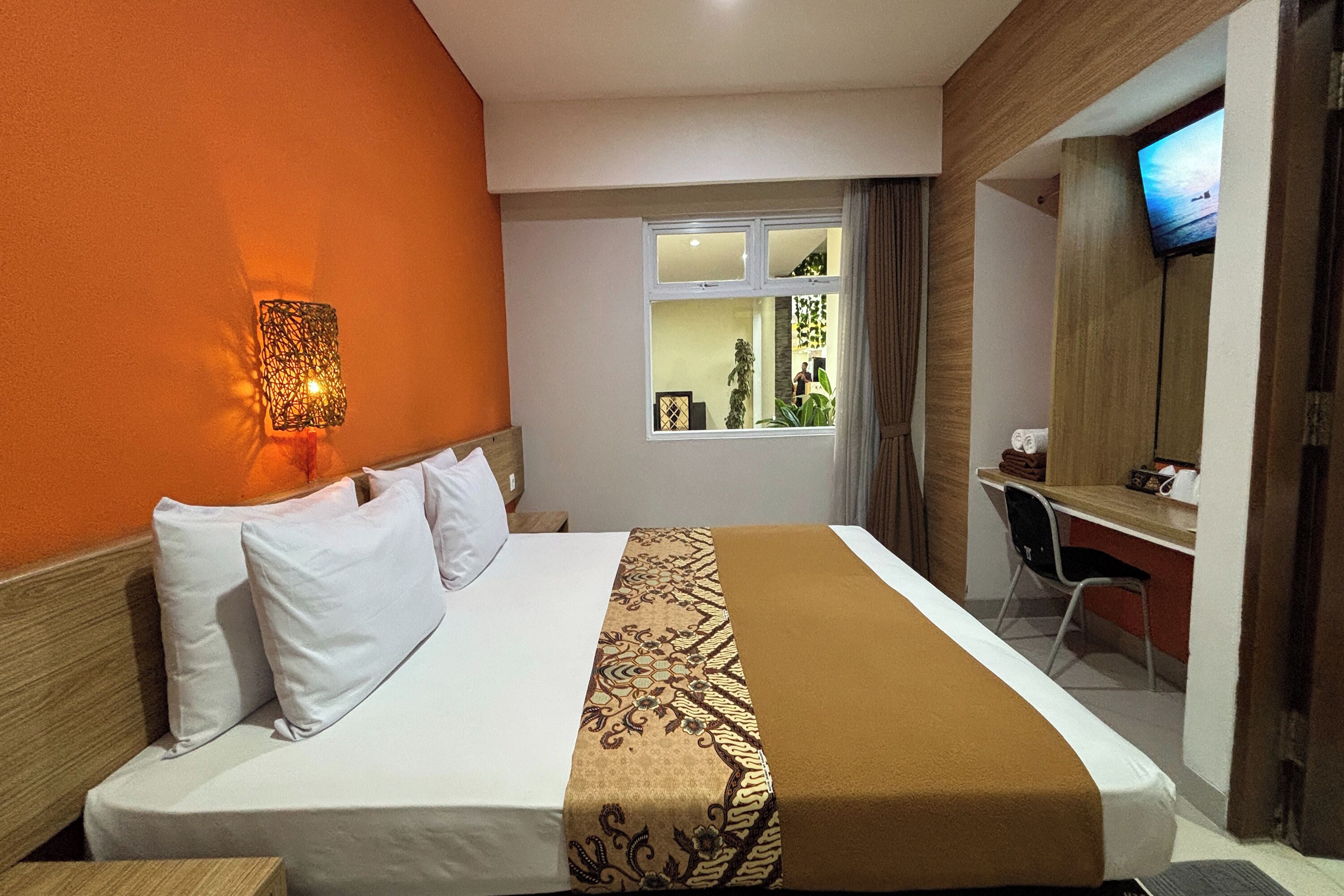 Quarto de hotel com cama, escrivaninha, televisão e janela com vista para o verde.
