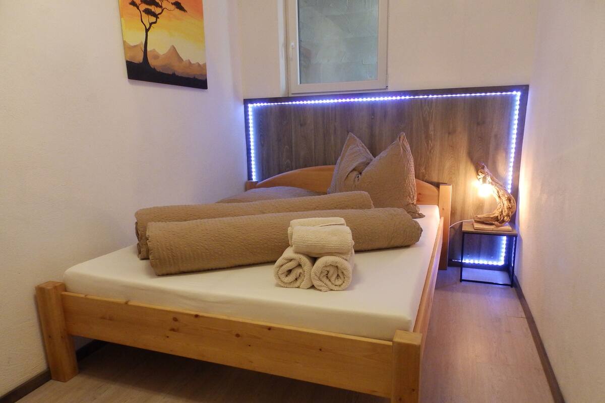 Uma cama bem arrumada com toalhas, uma mesa de cabeceira com abajur, e um quadro na parede.
