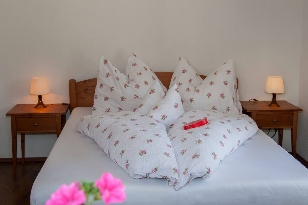 Uma cama bem arrumada com roupa de cama floral, duas mesas de cabeceira com abajures e uma cabeceira de madeira.