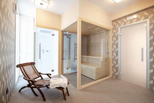 Quarto de hotel moderno com uma cadeira de madeira, box de chuveiro de vidro e um móvel de armazenamento bem organizado.