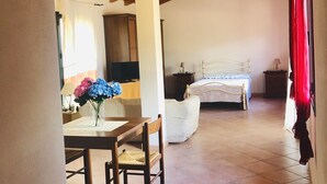 Um quarto amplo com teto de madeira alto, uma cama, uma mesa de jantar com cadeiras e uma janela com cortinas.