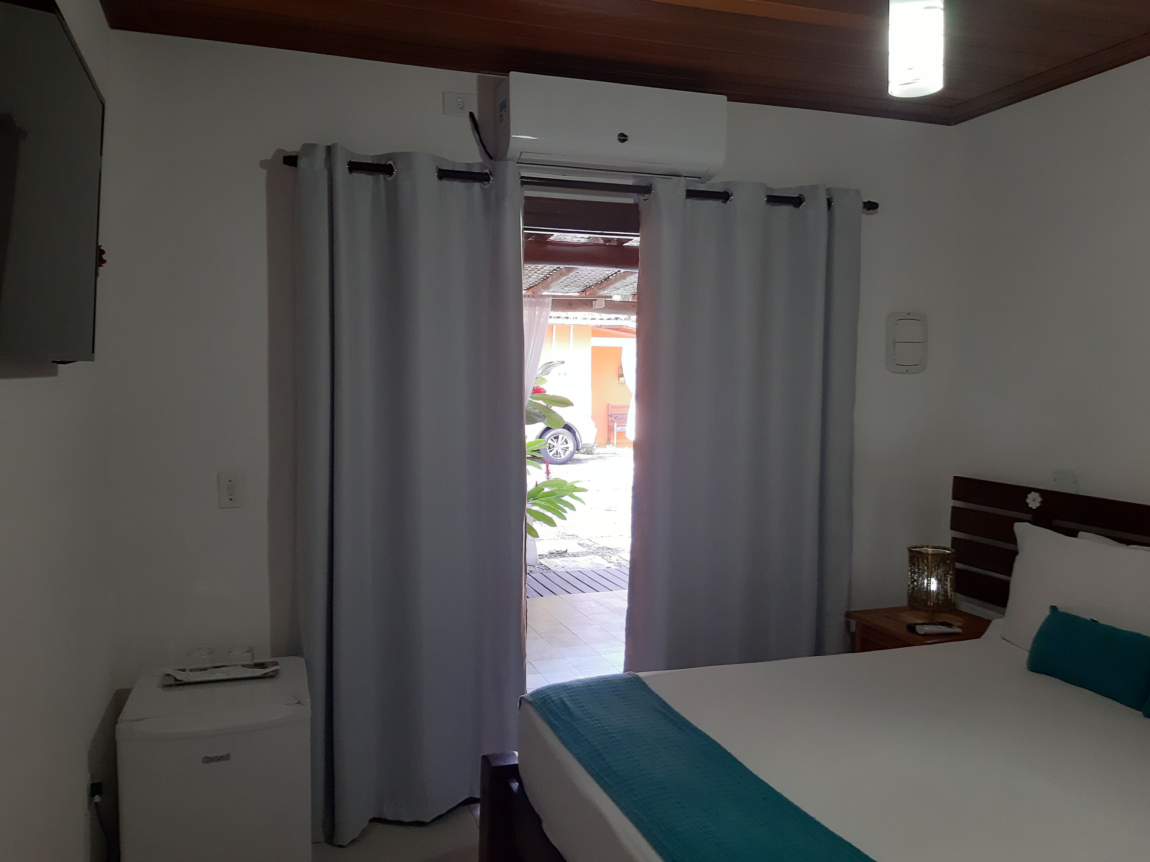 Quarto de hotel com cama, mesa de cabeceira com abajur e janela com cortinas.