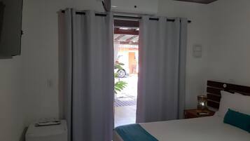 Quarto de hotel com cama, mesa de cabeceira com abajur e janela com cortinas.