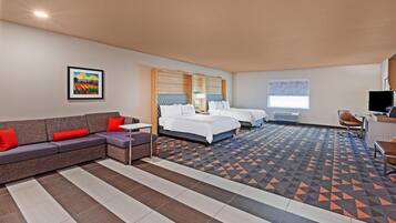 Quarto de hotel com sofá, duas camas, escrivaninha, televisão e janela.