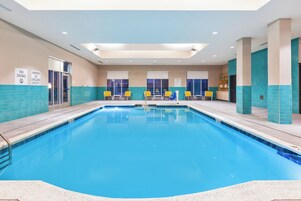 Piscina interna com água cristalina, cercada por áreas de estar e uma parede revestida de azulejos.