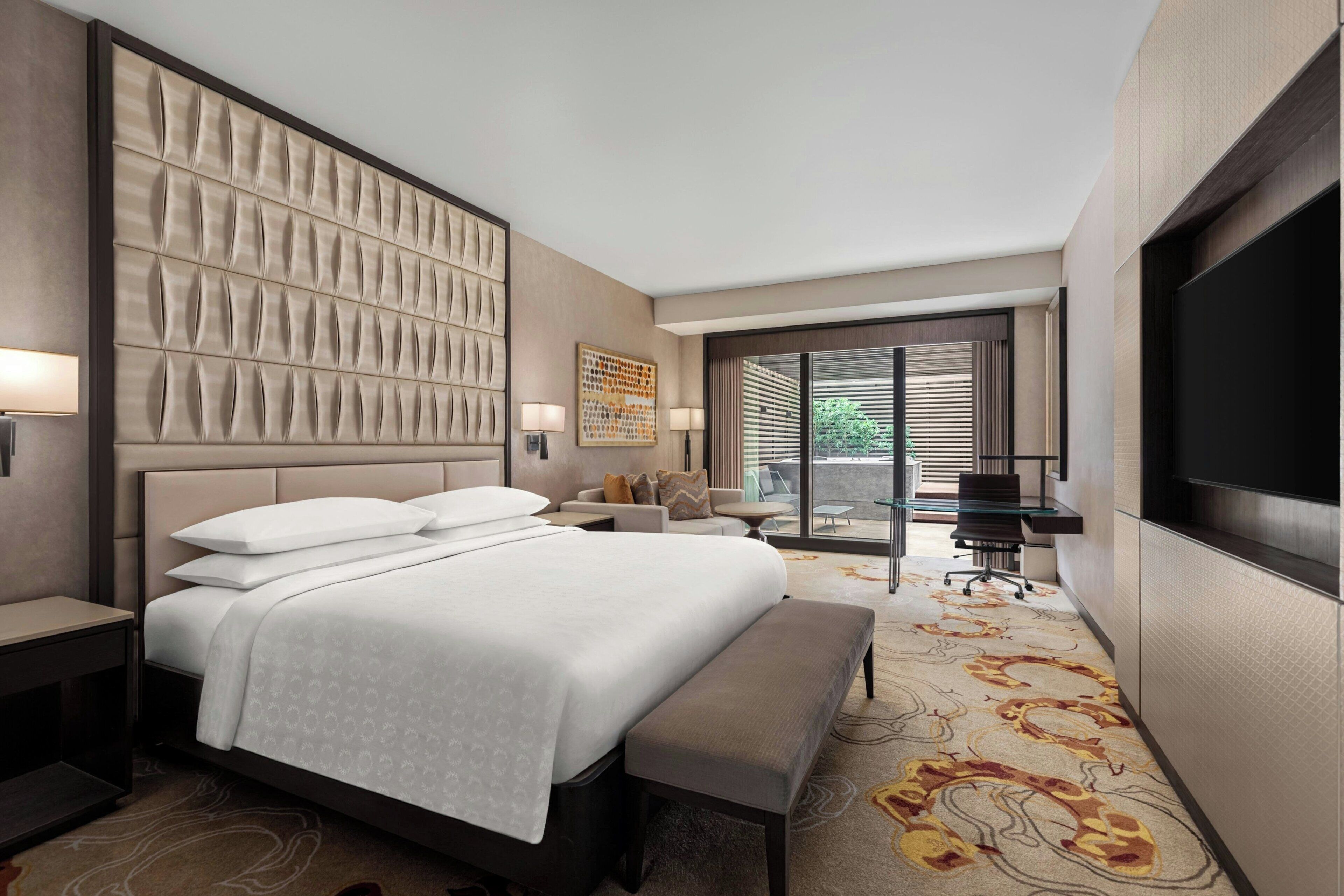 Quarto de hotel moderno com uma cama grande, uma escrivaninha e uma televisão.