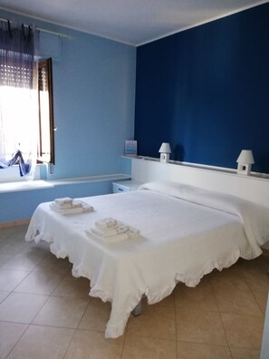 Quarto de hotel com duas camas, uma janela com cortinas, mesa de cabeceira e criado-mudo.