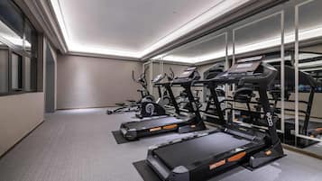 Uma academia com esteiras, elípticos e bicicletas ergométricas, piso coberto de carpete e uma parede de vidro.