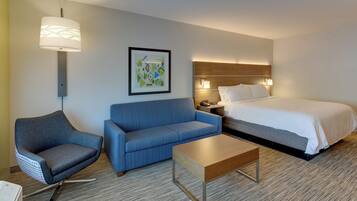 Quarto de hotel com cama, sofá, poltrona, mesinha e luminária na parede.