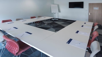 Uma sala de conferências com uma mesa grande, cadeiras, um quadro branco e uma porta.