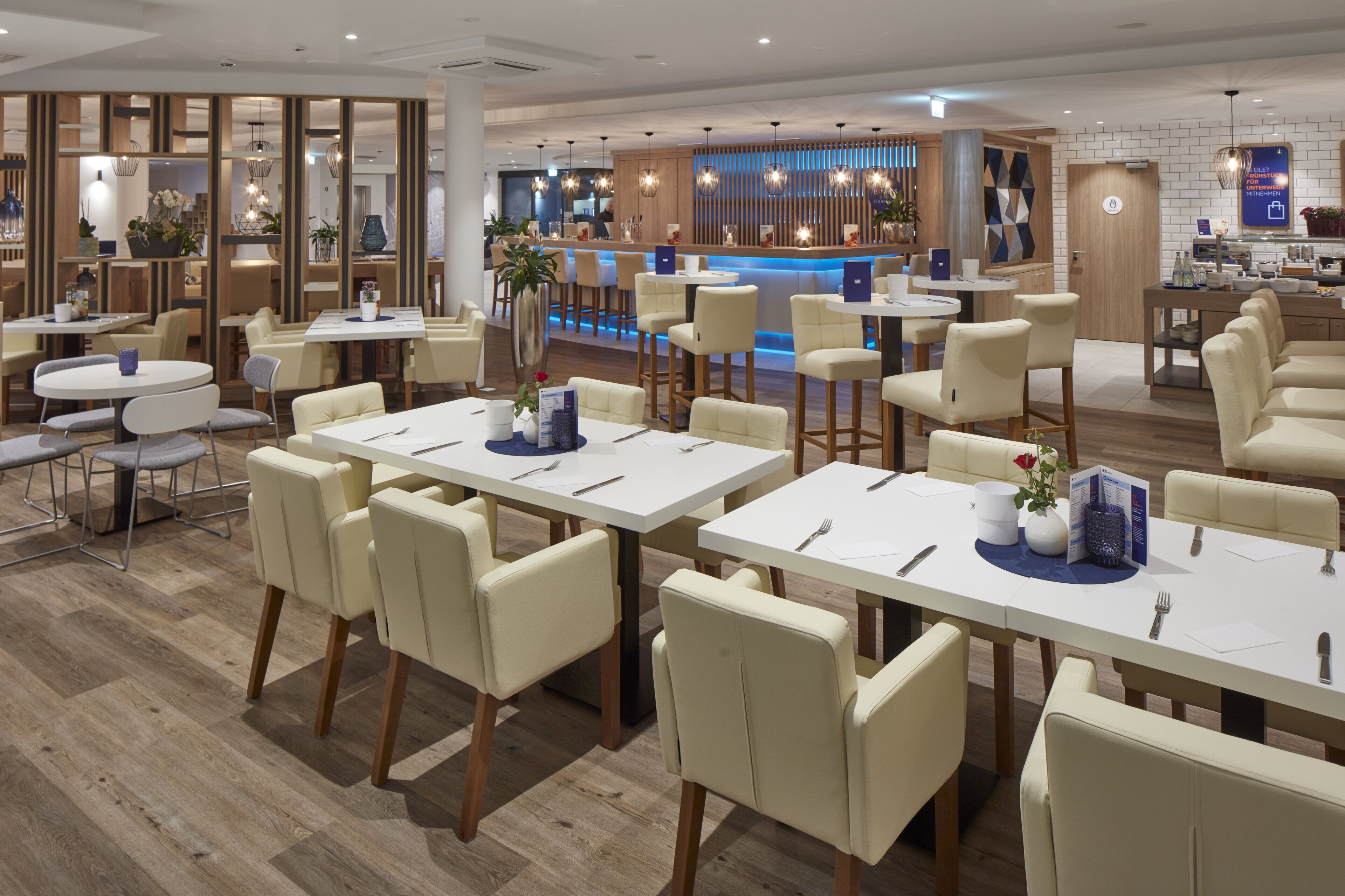 Um restaurante moderno com várias mesas e cadeiras, um espaço de bar e uma cozinha ao fundo.
