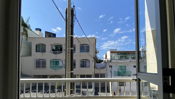 Uma varanda com vista para um conjunto de edifícios, incluindo uma estrutura alta com um mastro, sob um céu claro.