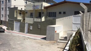 Edifício residencial com portão fechado, área externa coberta e varanda visível.
