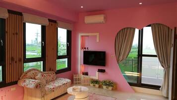 Uma sala de estar em tons de rosa com sofá, TV e janelas amplas.