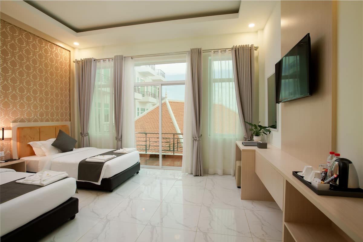 Quarto de hotel com duas camas, uma mesa de escritório, uma televisão e uma varanda com vista para a cidade.