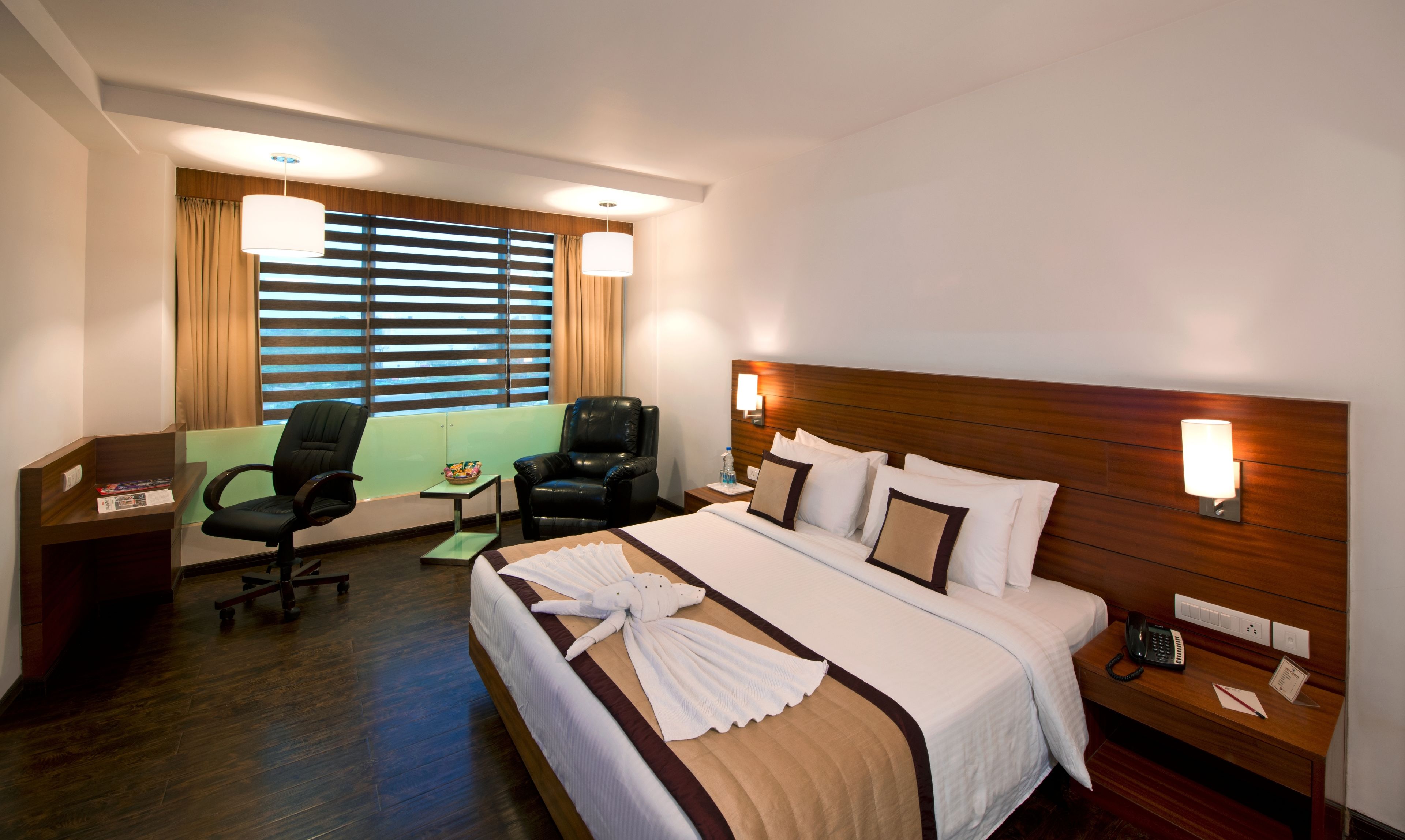 Quarto de hotel com uma cama grande, uma escrivaninha, uma cadeira e uma janela com persianas.