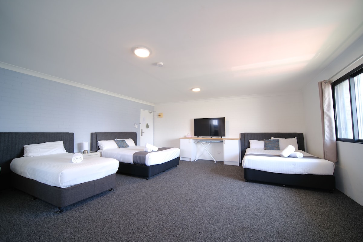Quarto de hotel com duas camas, uma escrivaninha, uma televisão e uma janela.